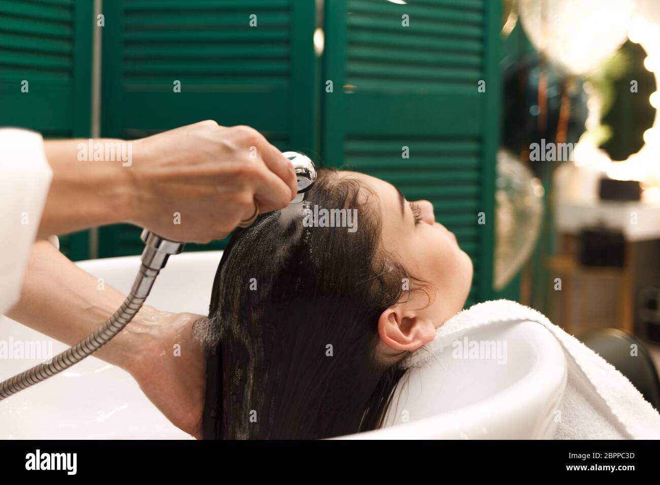 Beautiful young girl washes her head in a beauty studio. Hairdresser is ...