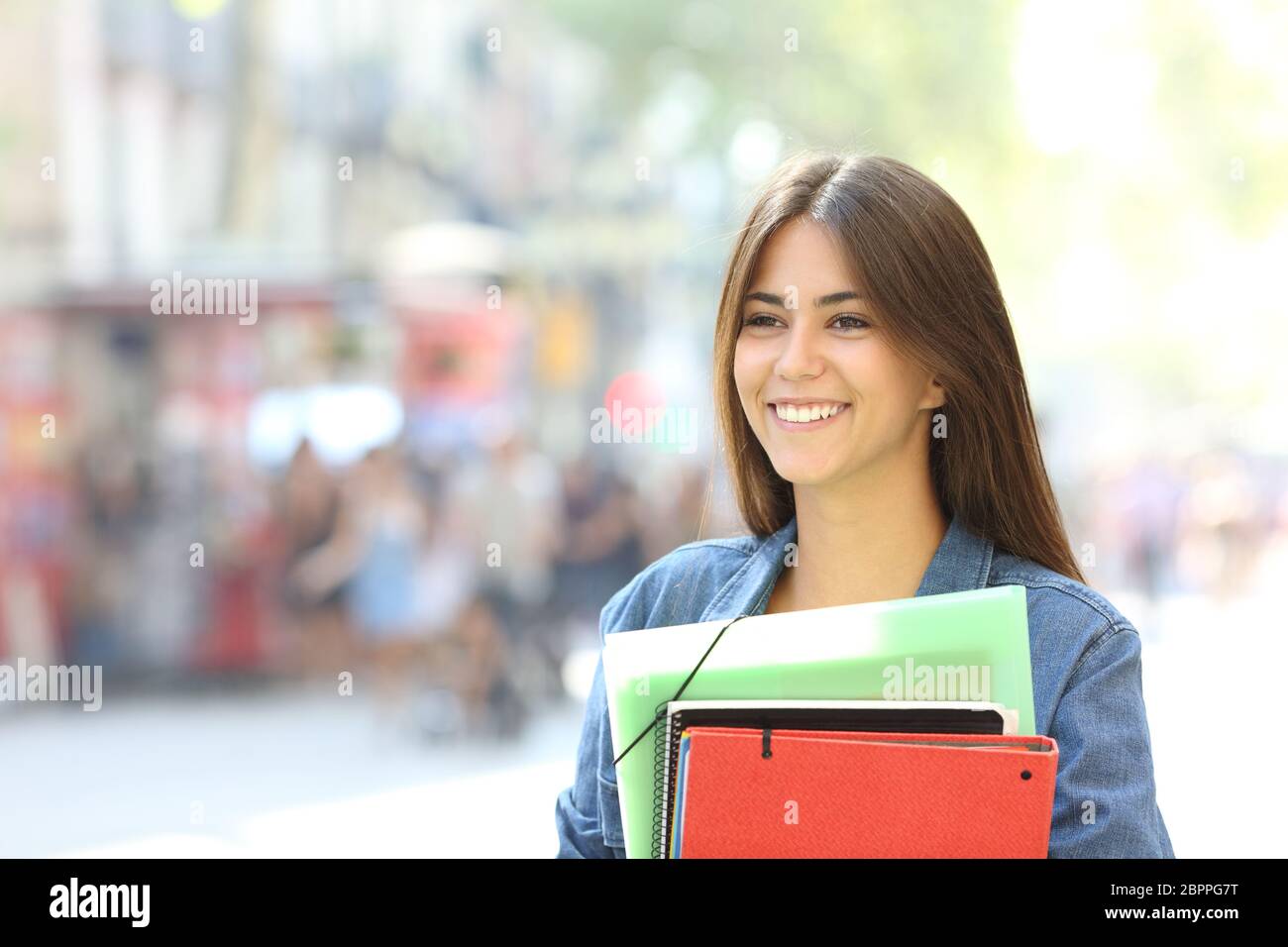 Happy student holding folders walking on the street Stock Photo - Alamy