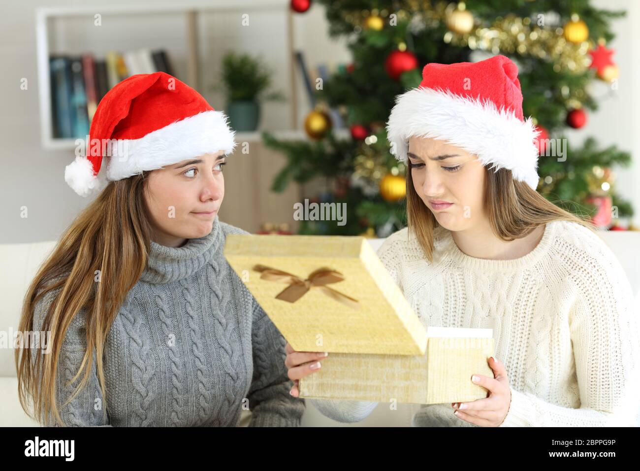 Disappointed woman receiving a gift from a frustrated friend in ...