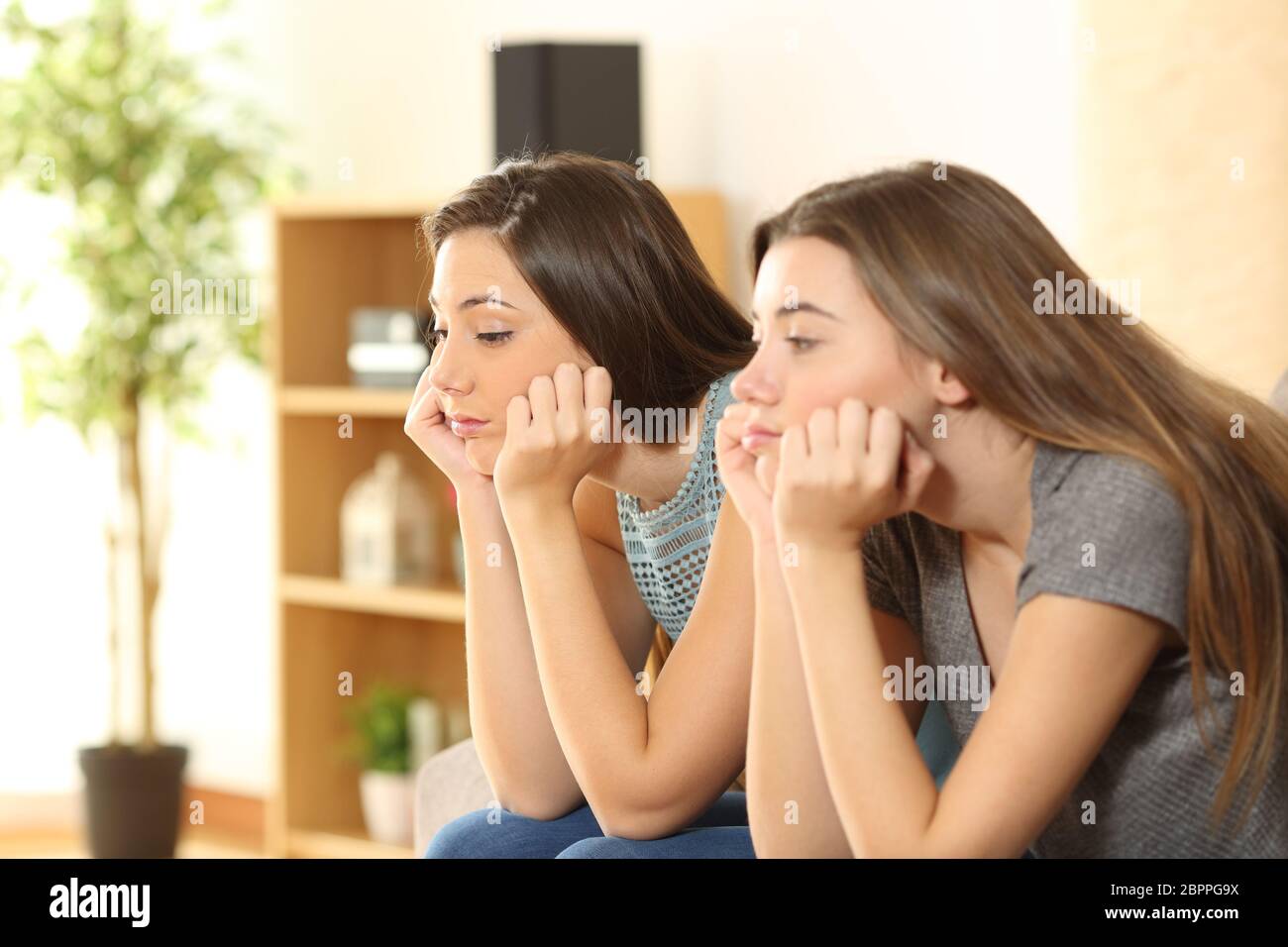 Bored roommates or friends sitting on a sofa in the living room at home ...
