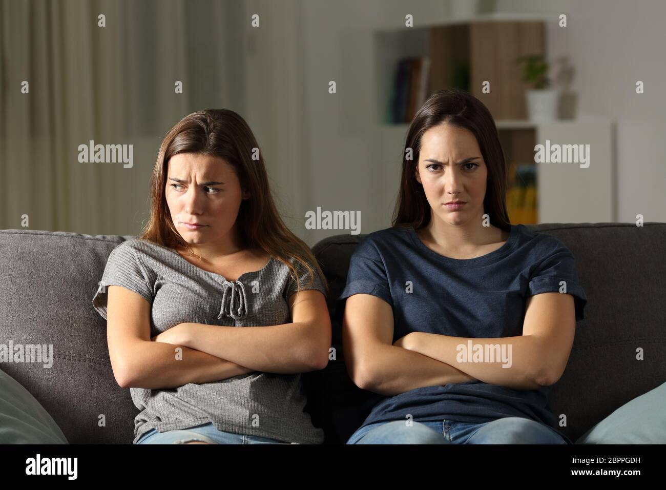 Angry woman looking at camera beside her friend sitting on a couch in ...
