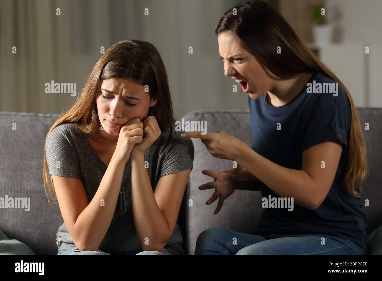 Angry woman scolding her sad friend sitting on a couch in the living ...