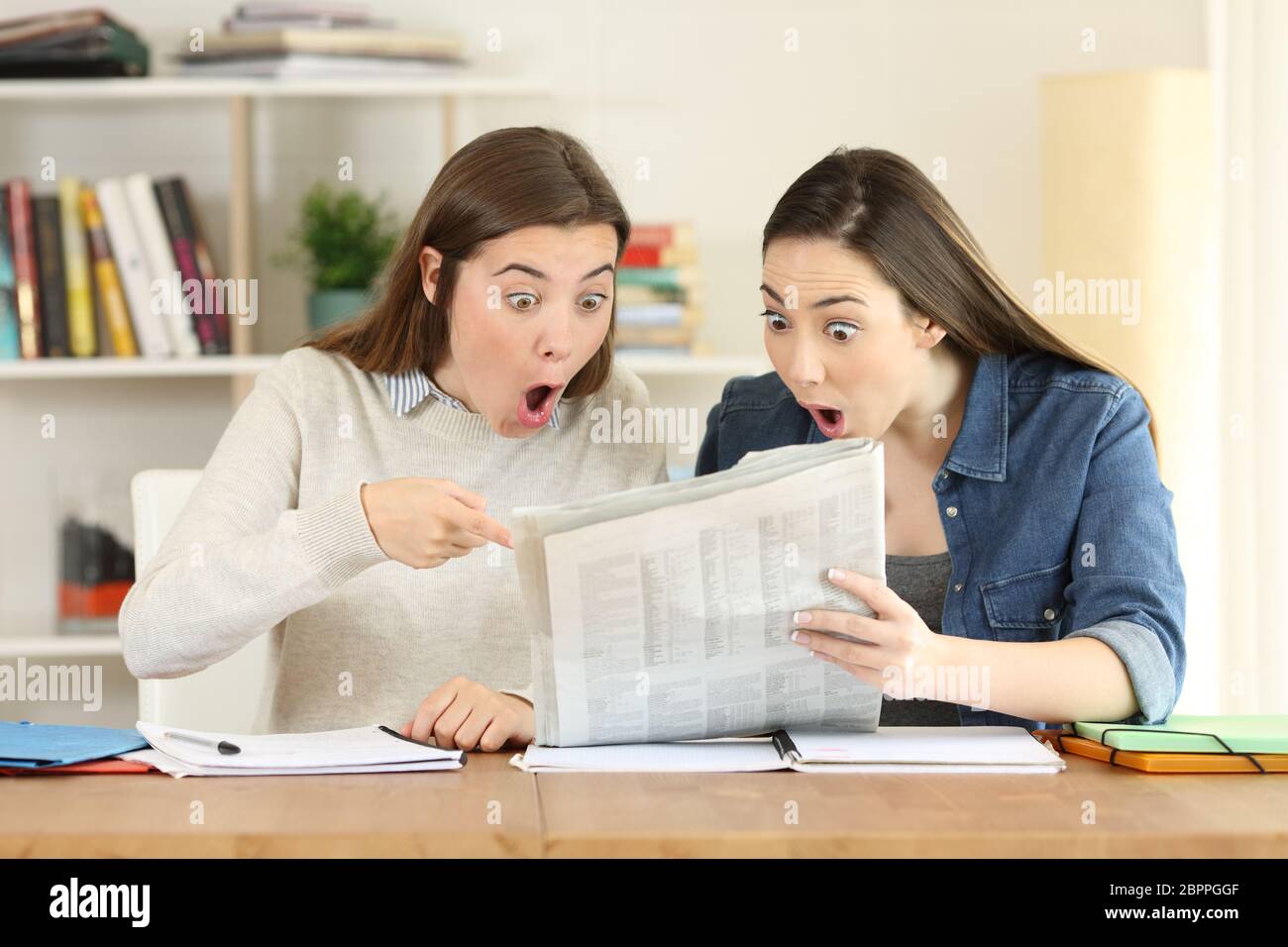 Two amazed students reading good news in a newspaper at home Stock ...