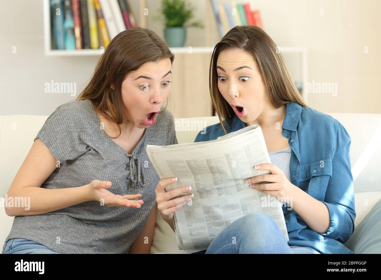 Amazed friends reading newspaper news sitting on a couch in the living ...