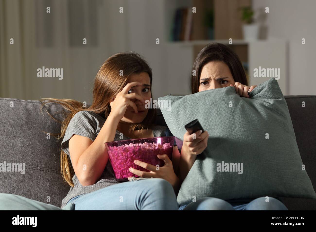 Terrified friends watching tv in the night sitting on a couch in the ...