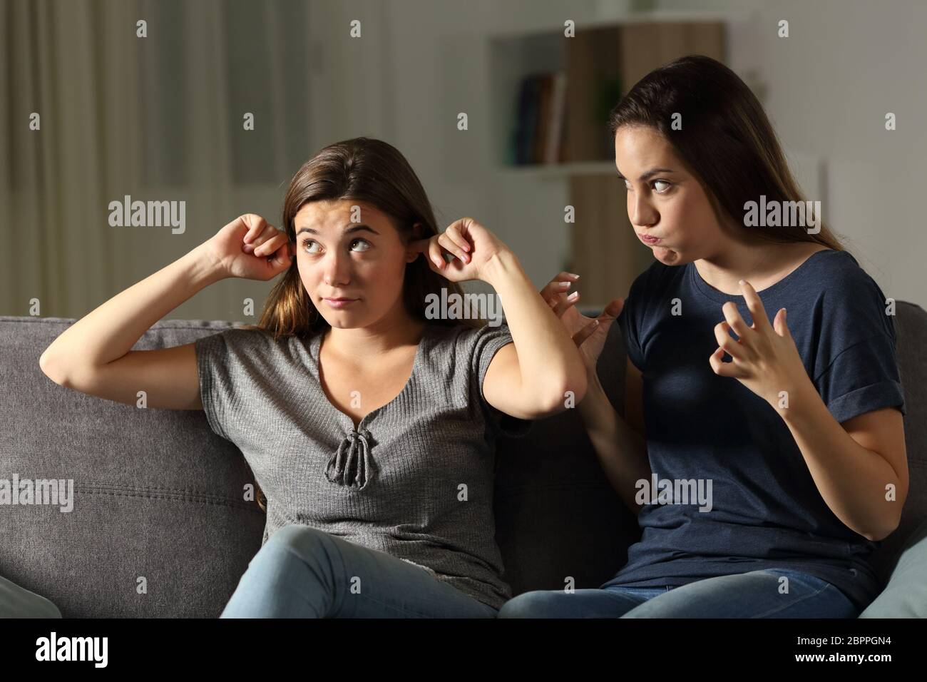 Furious woman and friend ignoring her sitting on a couch in the living ...