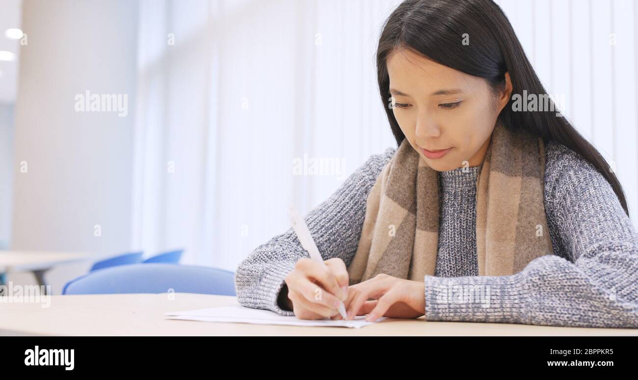 Woman student writing on note in library Stock Photo - Alamy