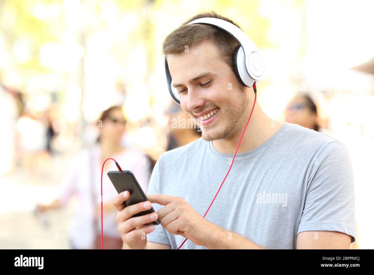 Happy boy listening to music and selecting a song walking on the street ...