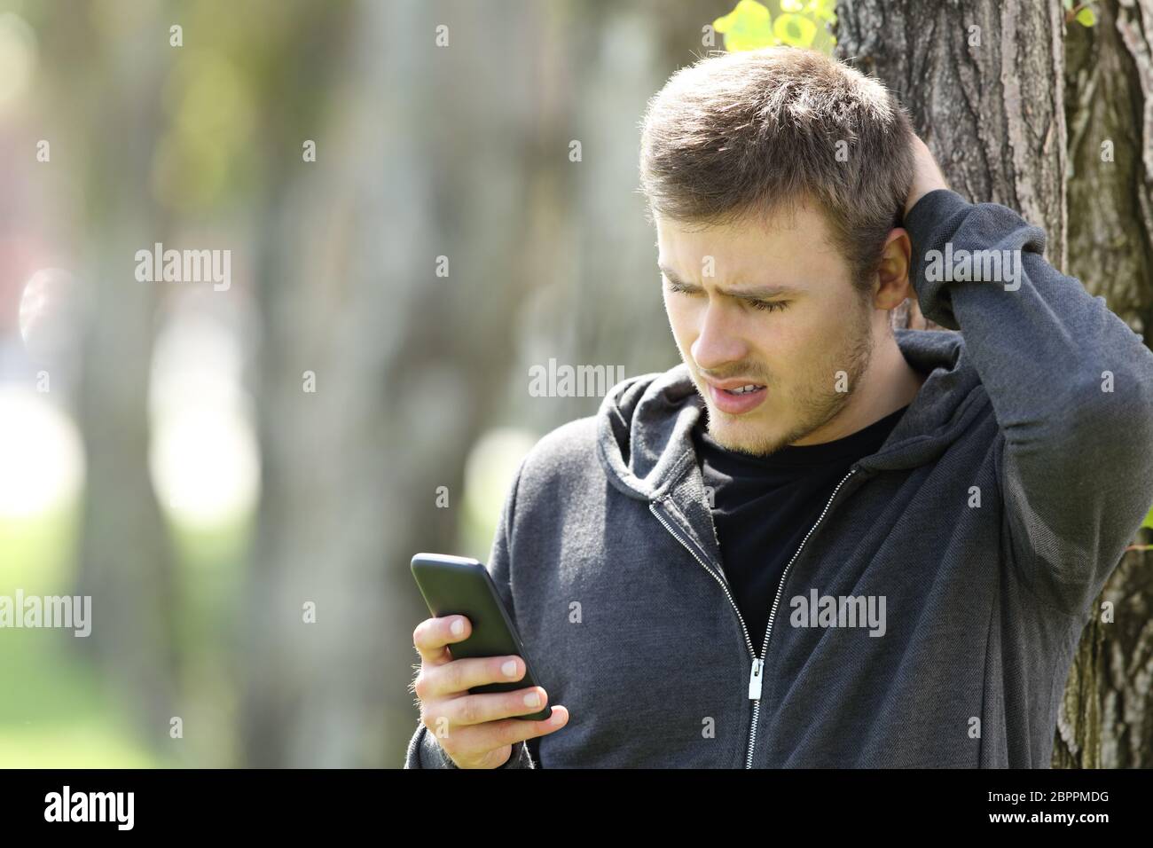 Confused single teen reading a message in a smart phone outdoors in a ...