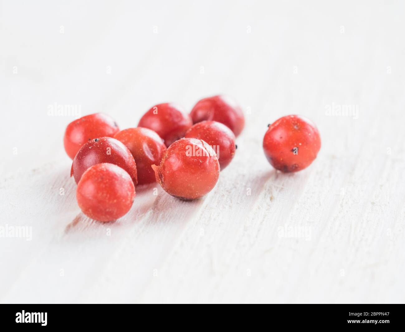 Heap of dried pink pepper berries on white wooden table. Close up view ...