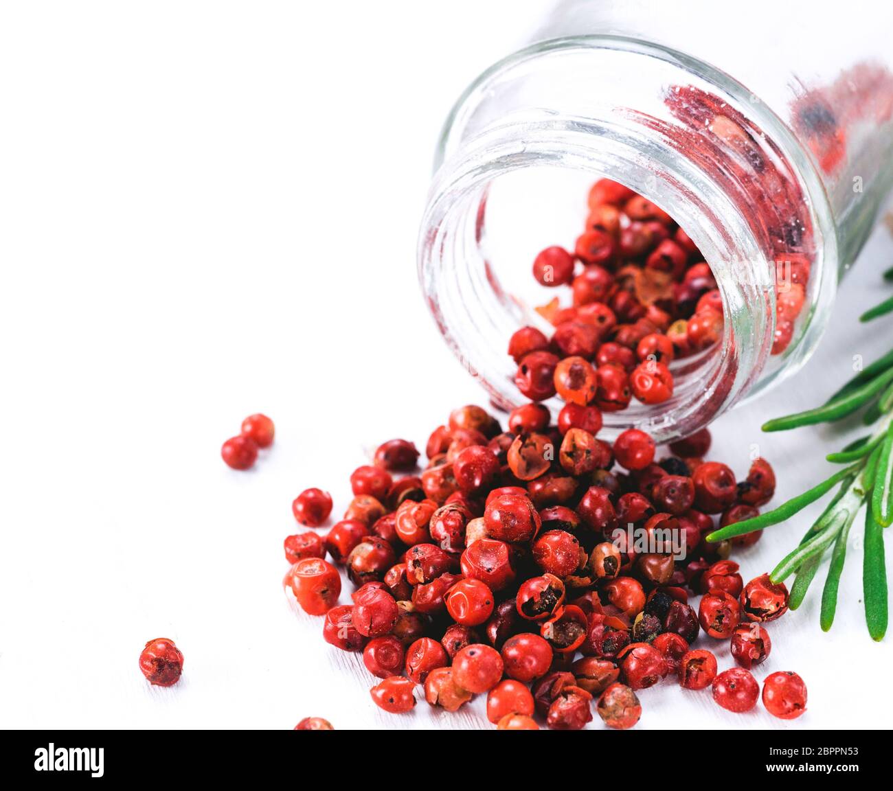 Dried pink pepper berries poured from glass jar on white wooden cutting ...