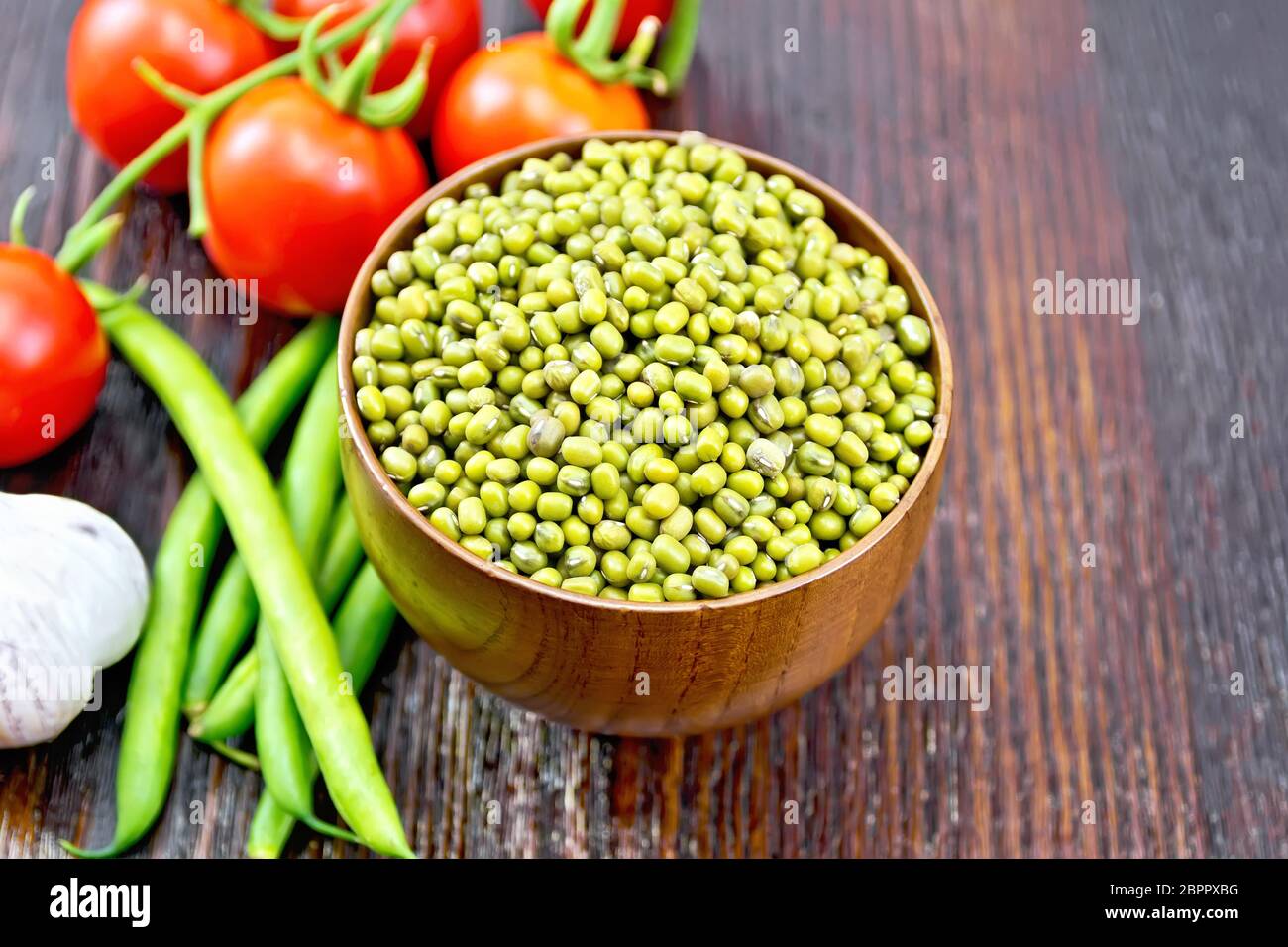 Green lentils mung in a bowl, pods of beans, garlic and red tomatoes on ...