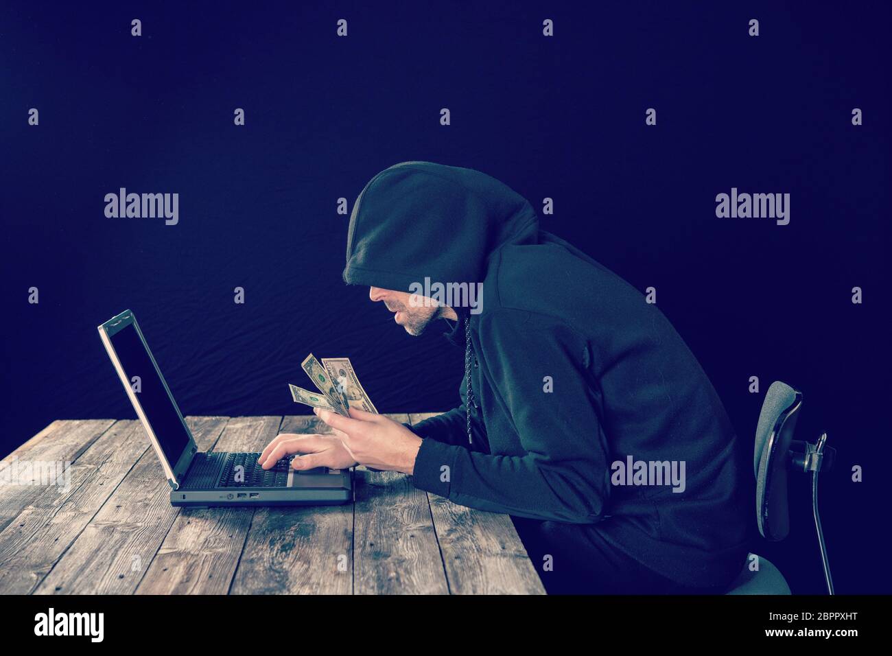 hacker in black hoody with laptop and dollar notes in front of black ...