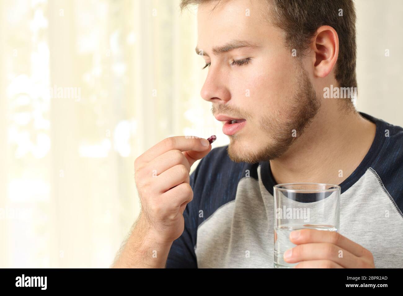 Serious man taking a pill standing at home Stock Photo - Alamy