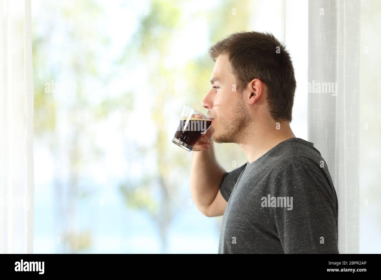 Side view of a man drinking coffee looking through the window of home ...