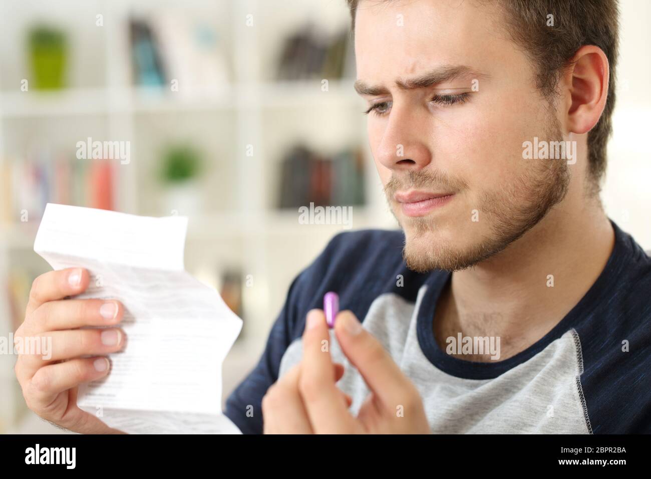 Suspicious man reading the leaflet of a pill sitting on a couch at home ...