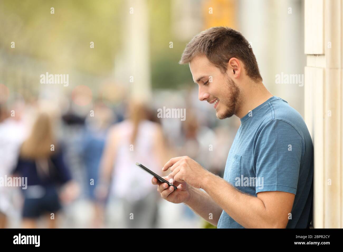 Side view of a happy guy texting on a smart phone leaning on a wall on ...