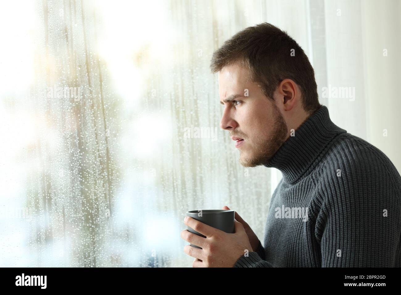 Side view portrait of an angry man looking outdoors through a window in ...