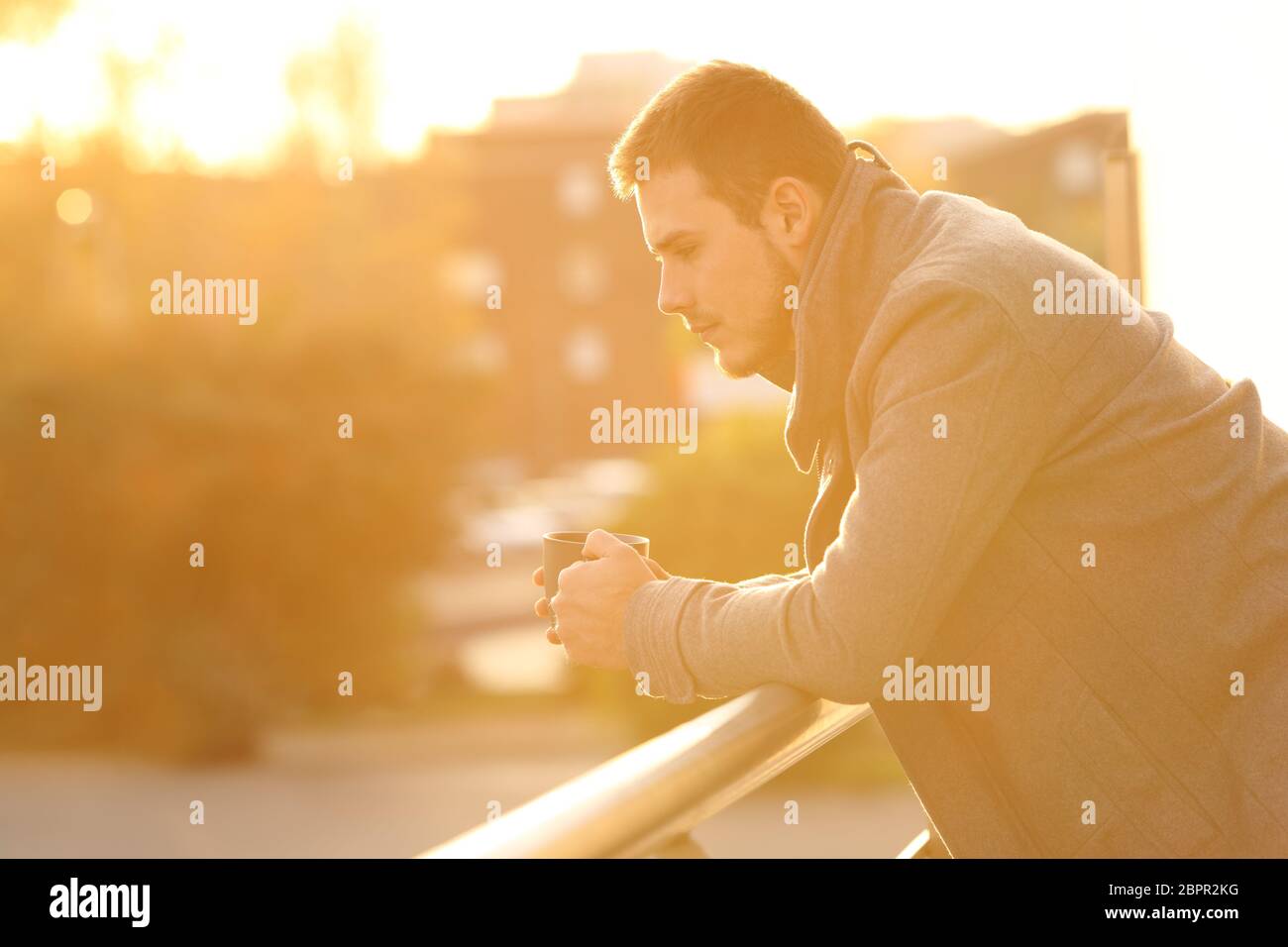 Side view portrait of a sad man looking down in a balcony at sunset in ...