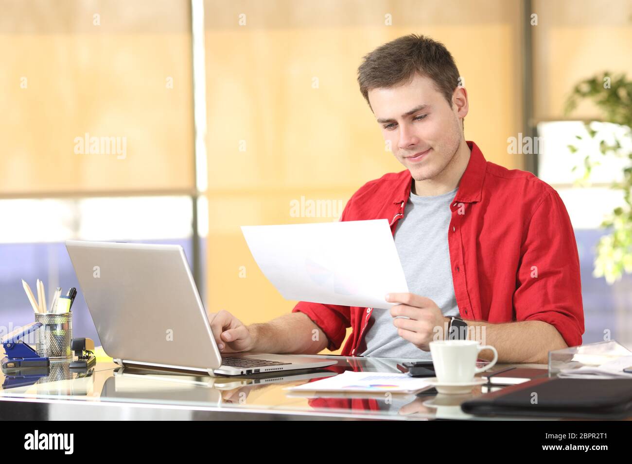 Entrepreneur working using a laptop and consulting documents sitting in ...