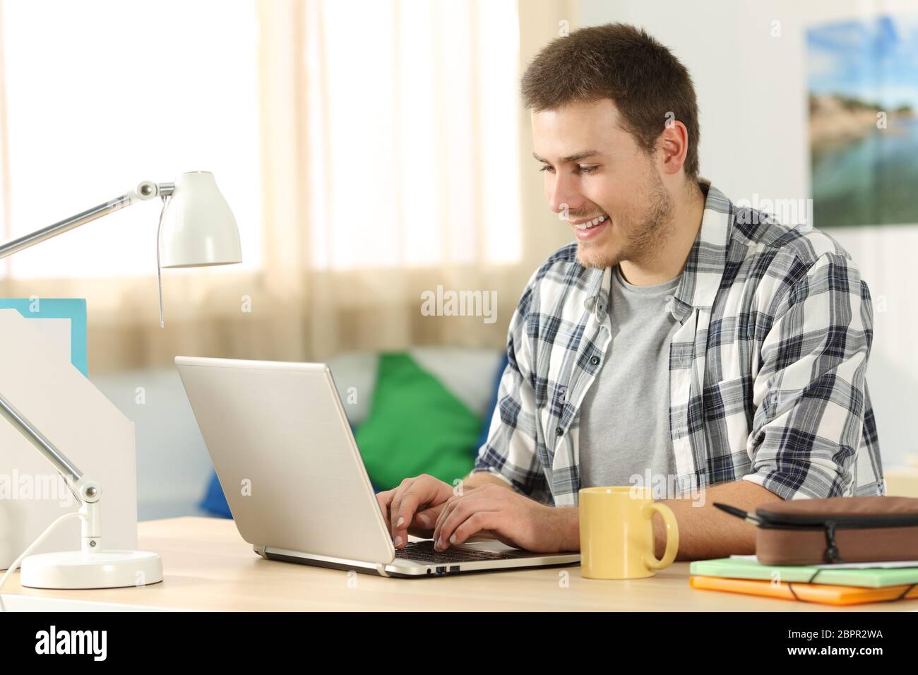 Happy student writing in a laptop sitting on a desk in his room Stock ...