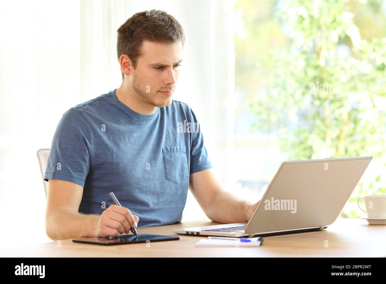 Serious man drawing with a display pen and a laptop on a desktop at ...