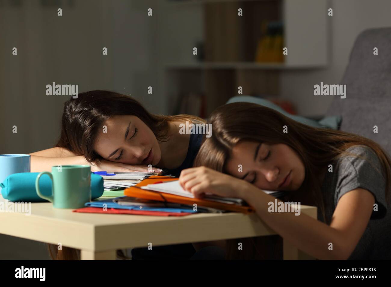Two tired students sleeping over notebooks after studying late hours in ...