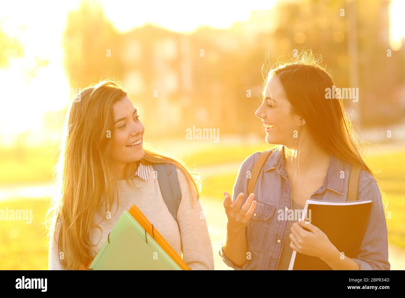 Front view portrait of two happy students walking and talking at sunset ...