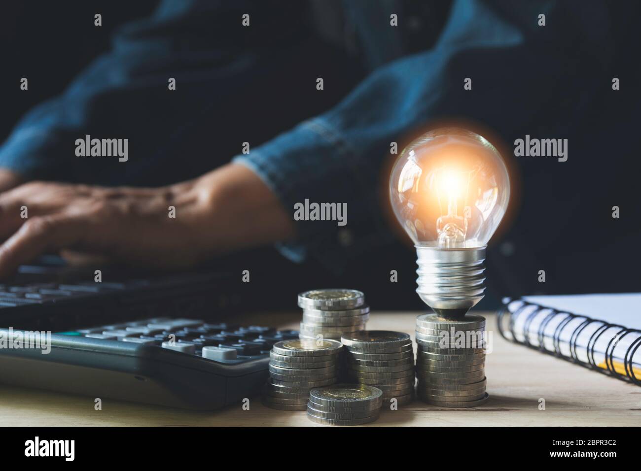 Man working with a light bulb on stack of coins for business and ...