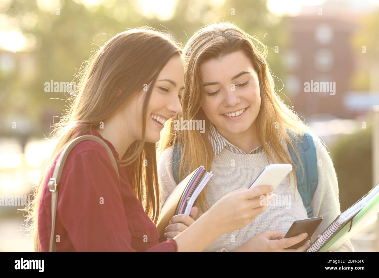 Two beautiful students watching media content on line in a smart phone ...