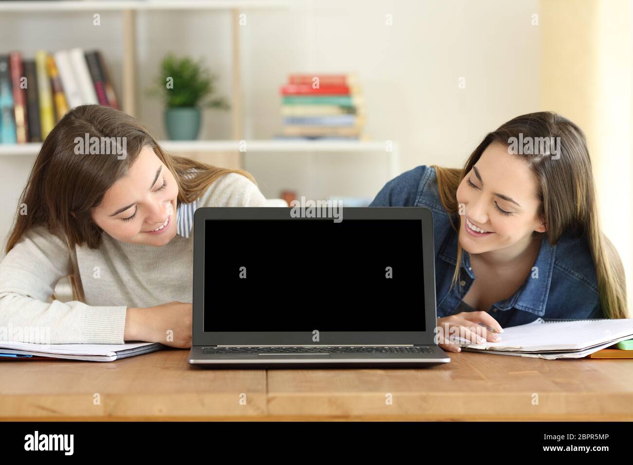 Two happy students watching a laptop mockup screen on a desk at home ...