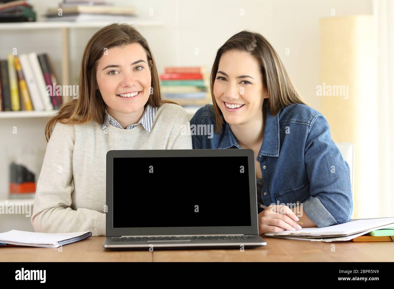 Front view portrait of two students showing a laptop screen mockup ...