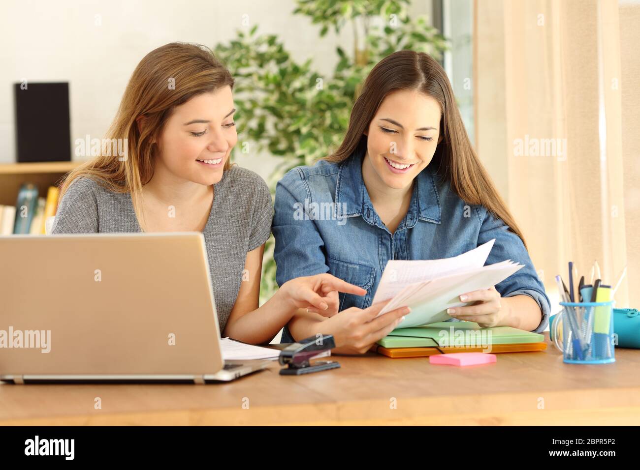 Two happy students studying checking and comparing notes on a desk at ...