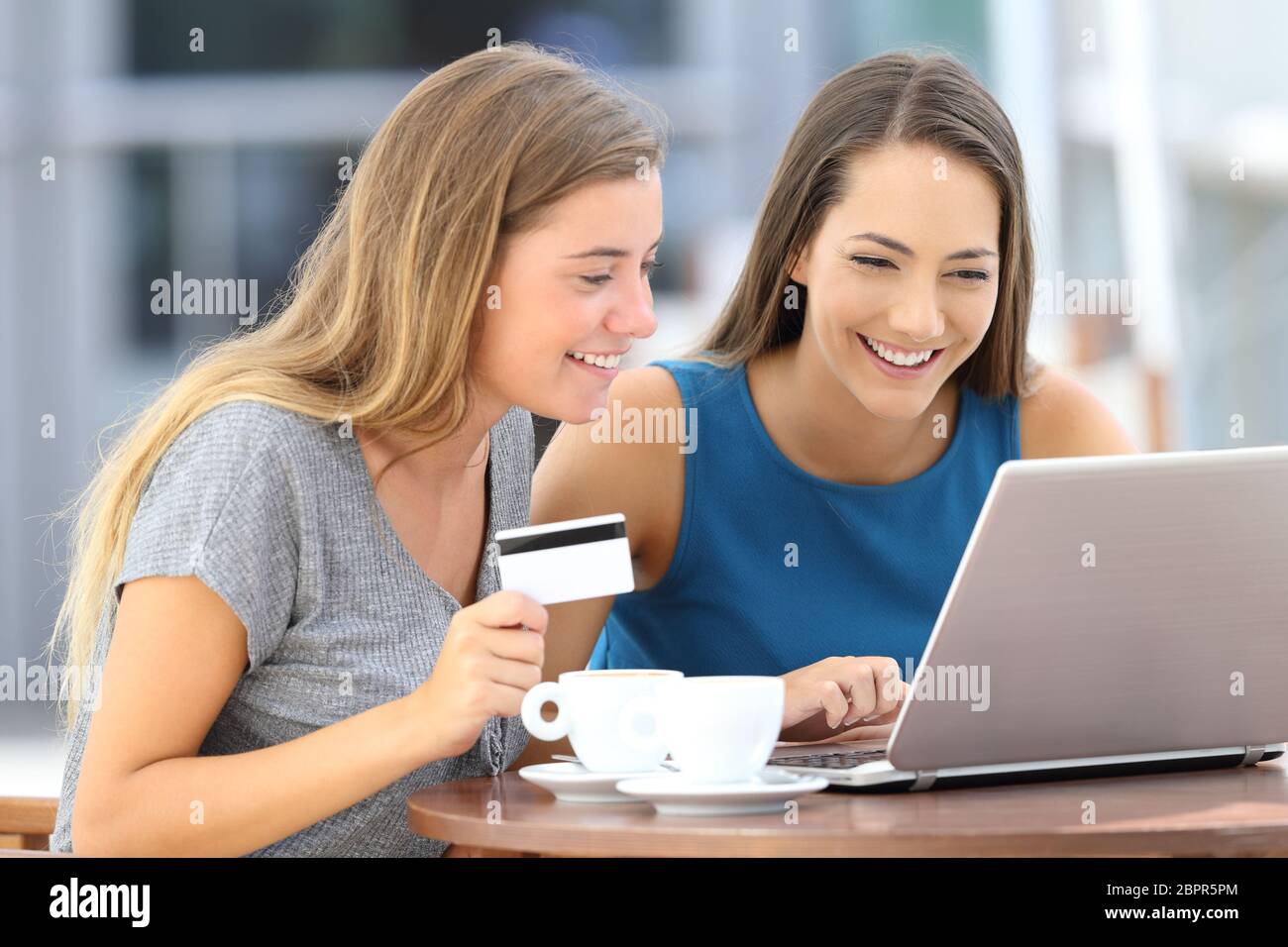 Two happy friends paying on line with a credit card and a laptop ...
