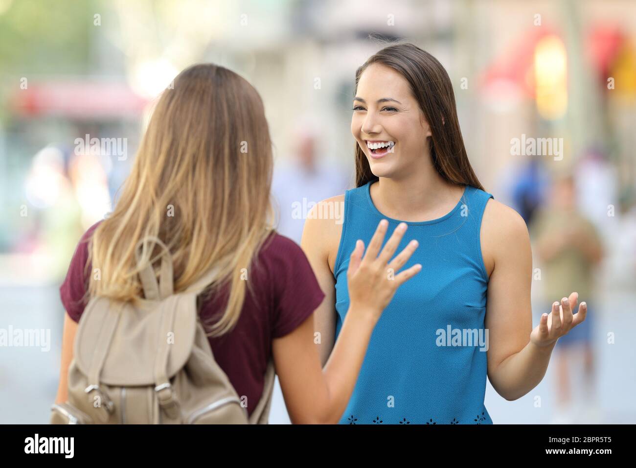 Two happy friends meeting and greeting on the street with a blurred ...