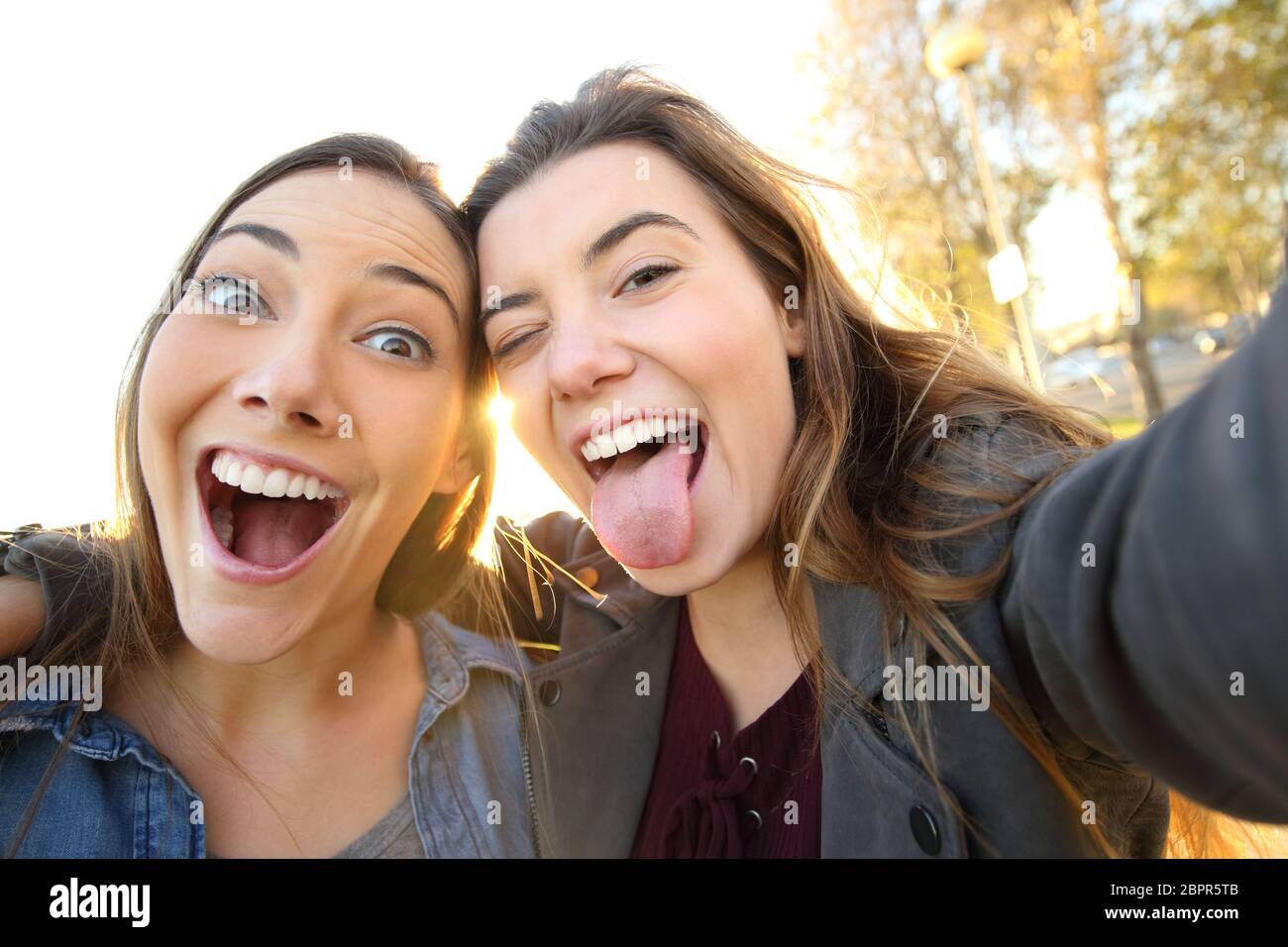 Two funny women joking taking selfies looking at camera in the street ...