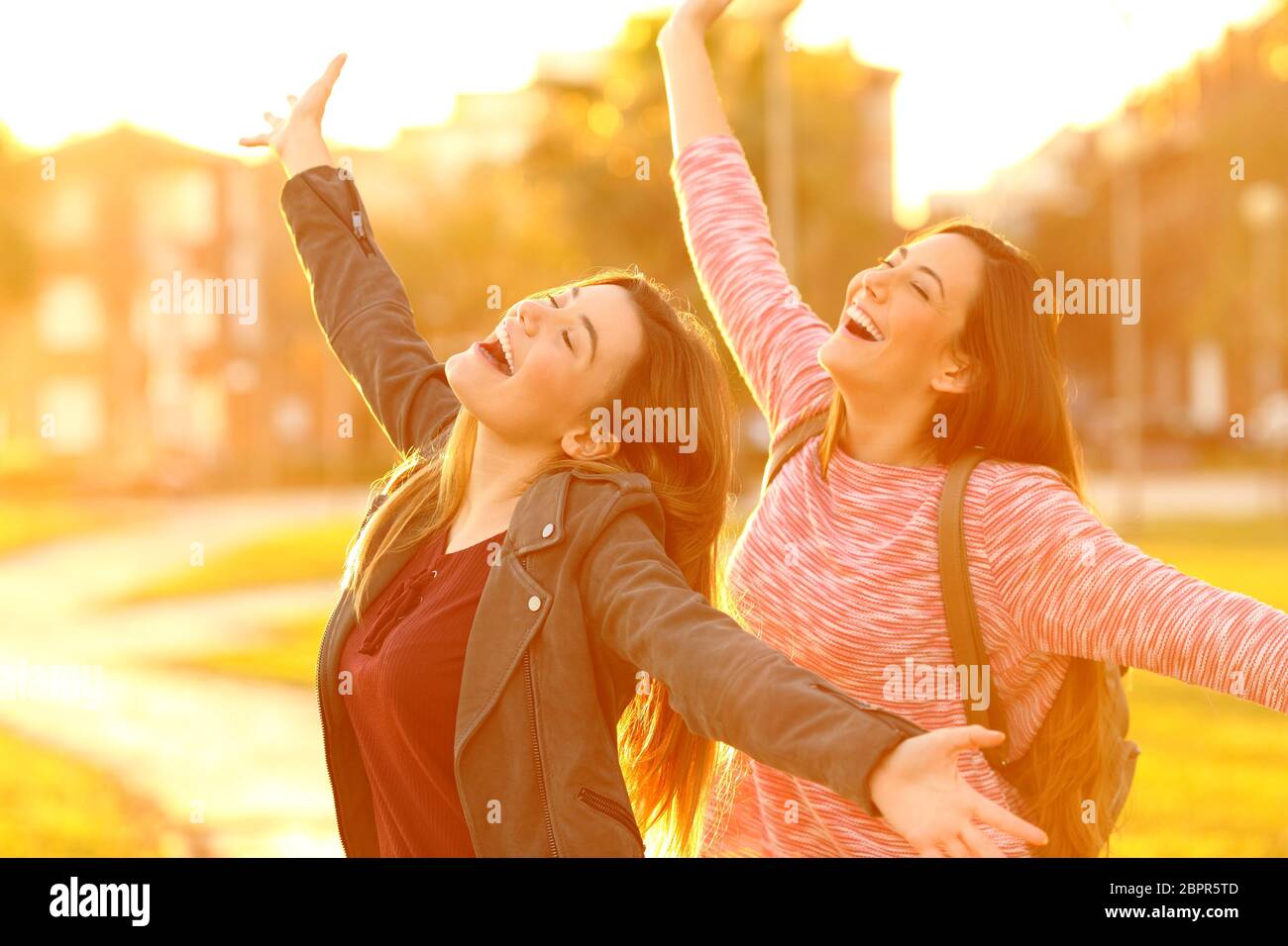 Joyful friends joking raising arms celebrating in a park at sunset ...