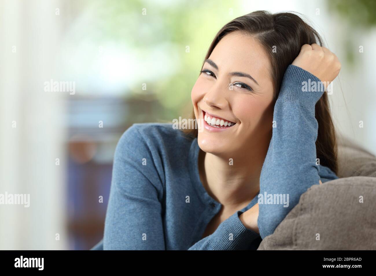 Happy woman looking at you with a perfect smile sitting on a couch in ...