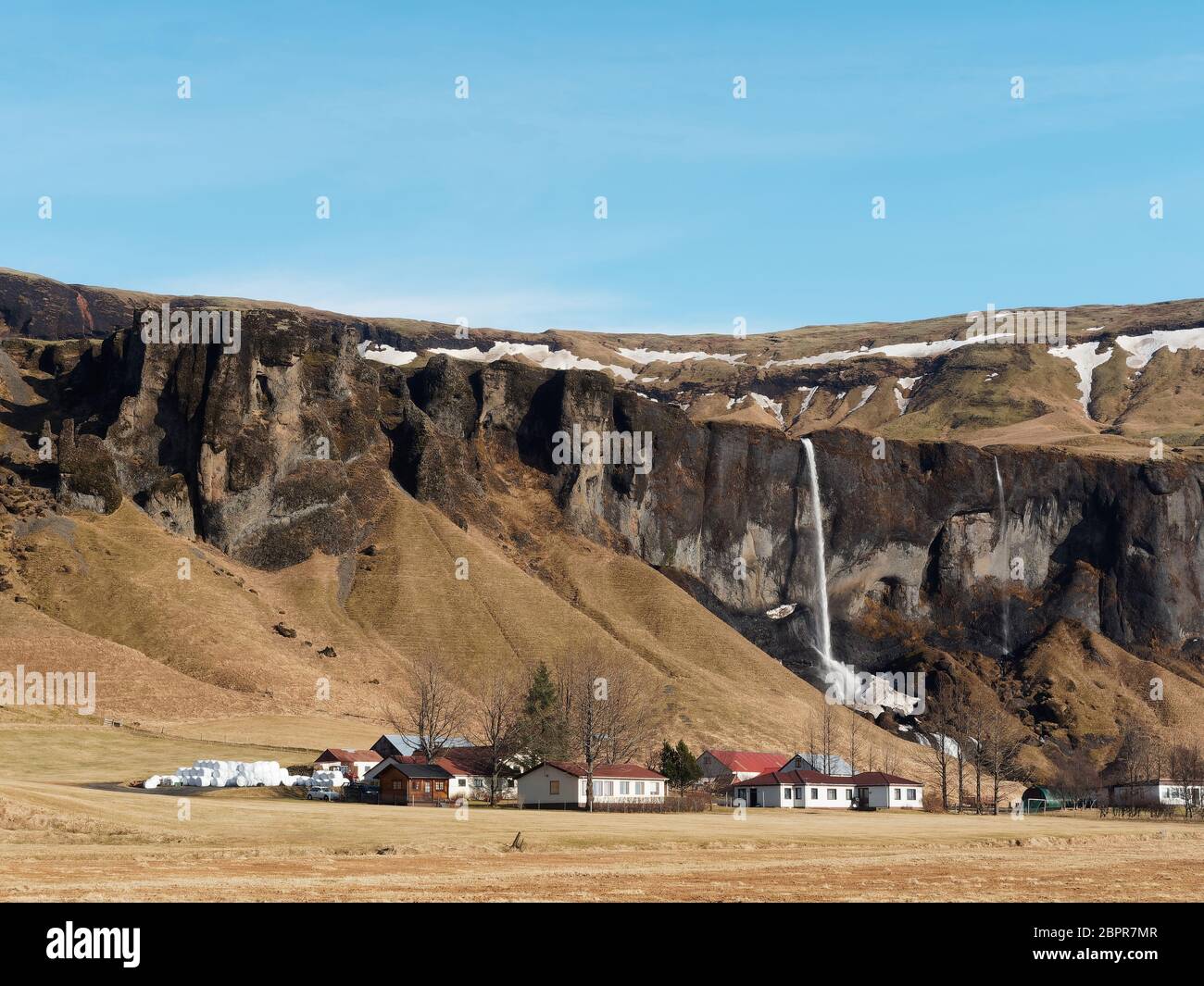 Basalt cliff, Foss a Sidu waterfall and farm, with blue sky in winter ...