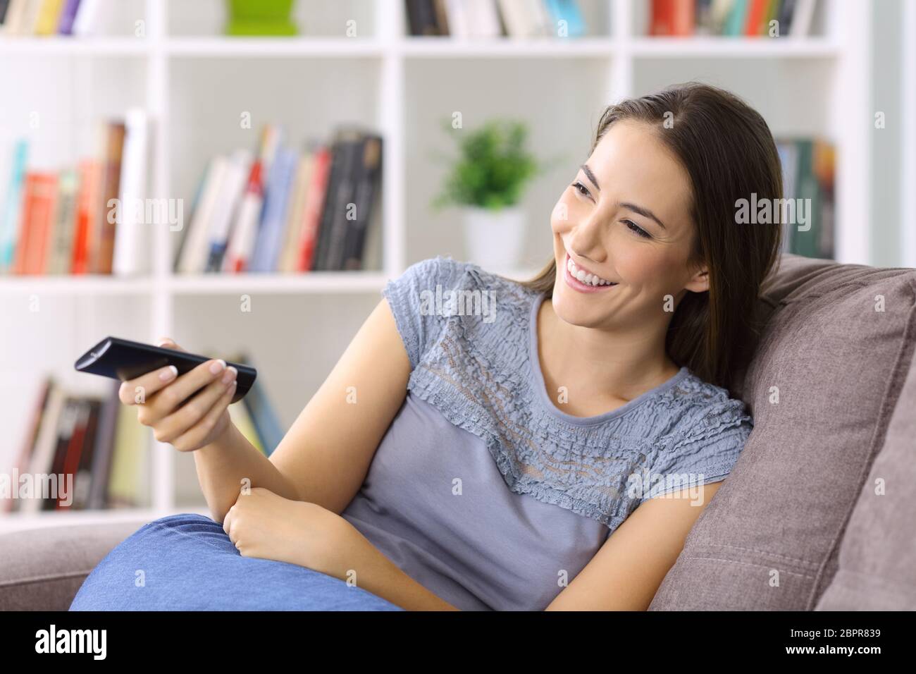 Happy lady watching tv and holding remote control sitting on a couch at ...