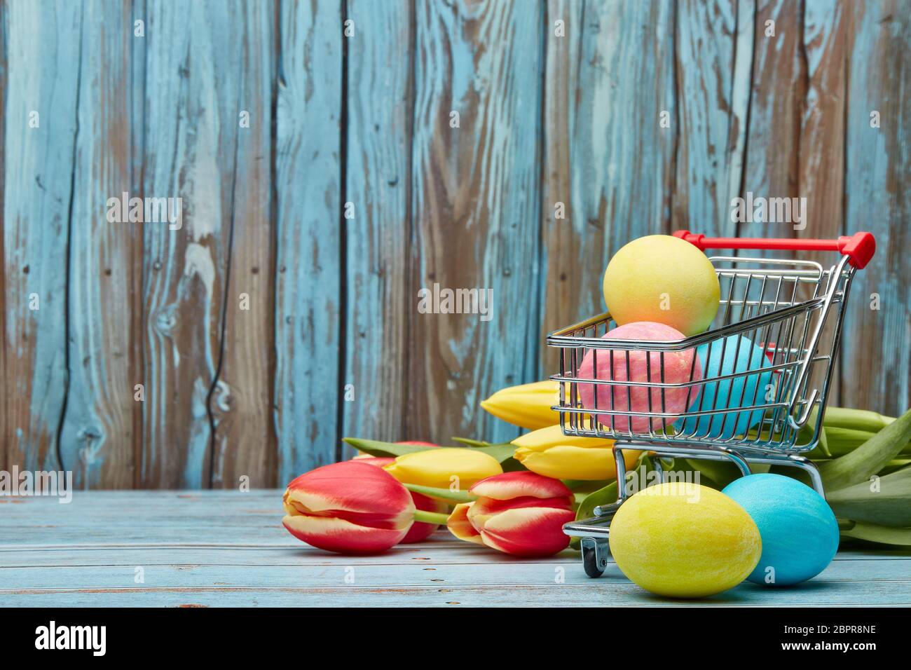 Colored easter eggs in shopping trolley and spring tulips flowers on a ...