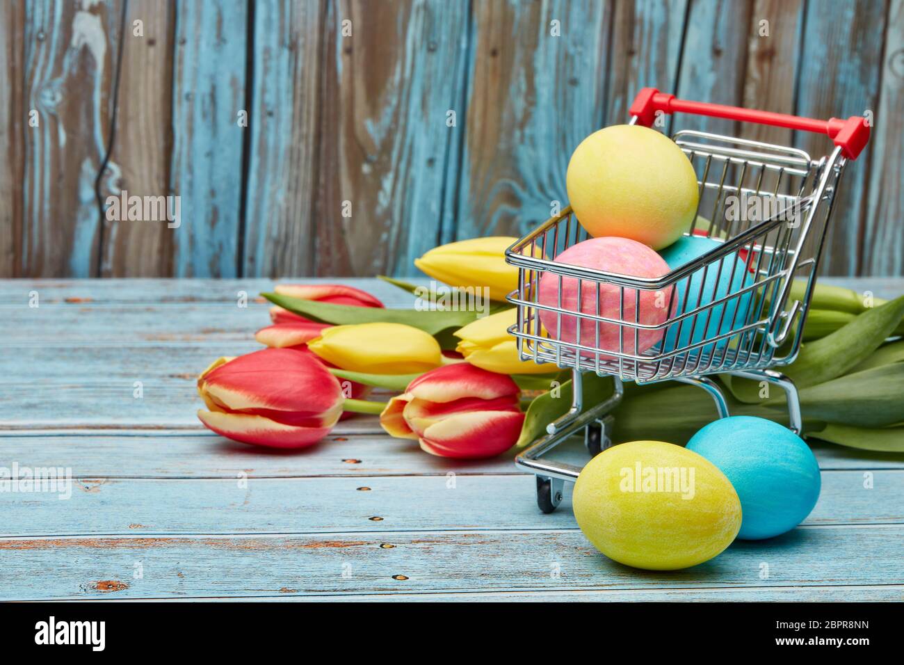 Colored easter eggs in shopping trolley and spring tulips flowers on a ...