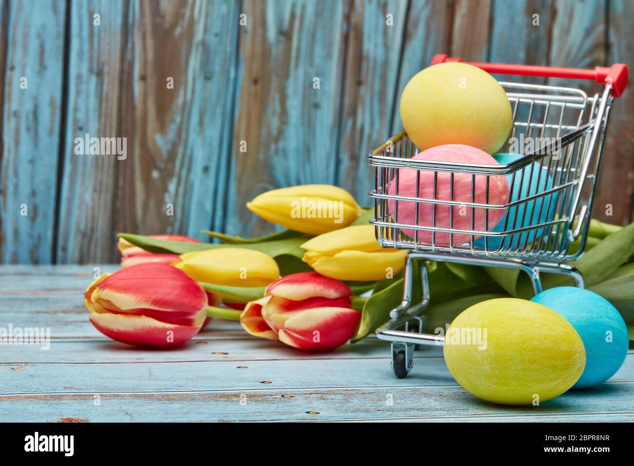 Colored easter eggs in shopping trolley and spring tulips flowers on a ...