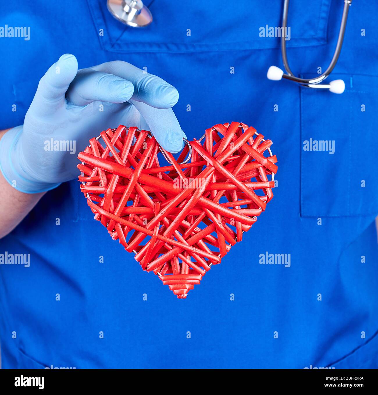 doctor in blue uniform and sterile latex gloves holds a big red heart ...