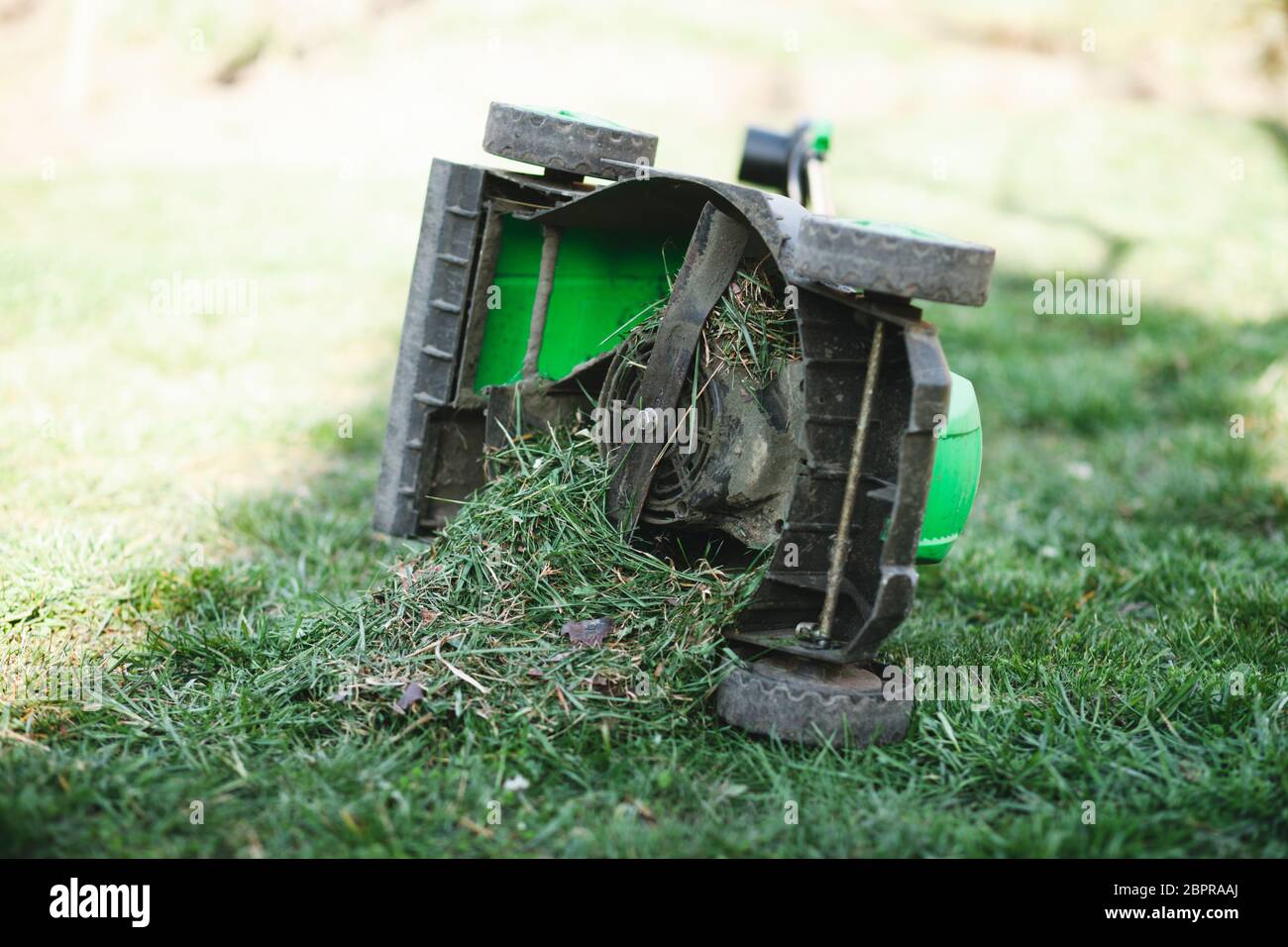Lawn mower overflowing with grass lies on its side Stock Photo - Alamy