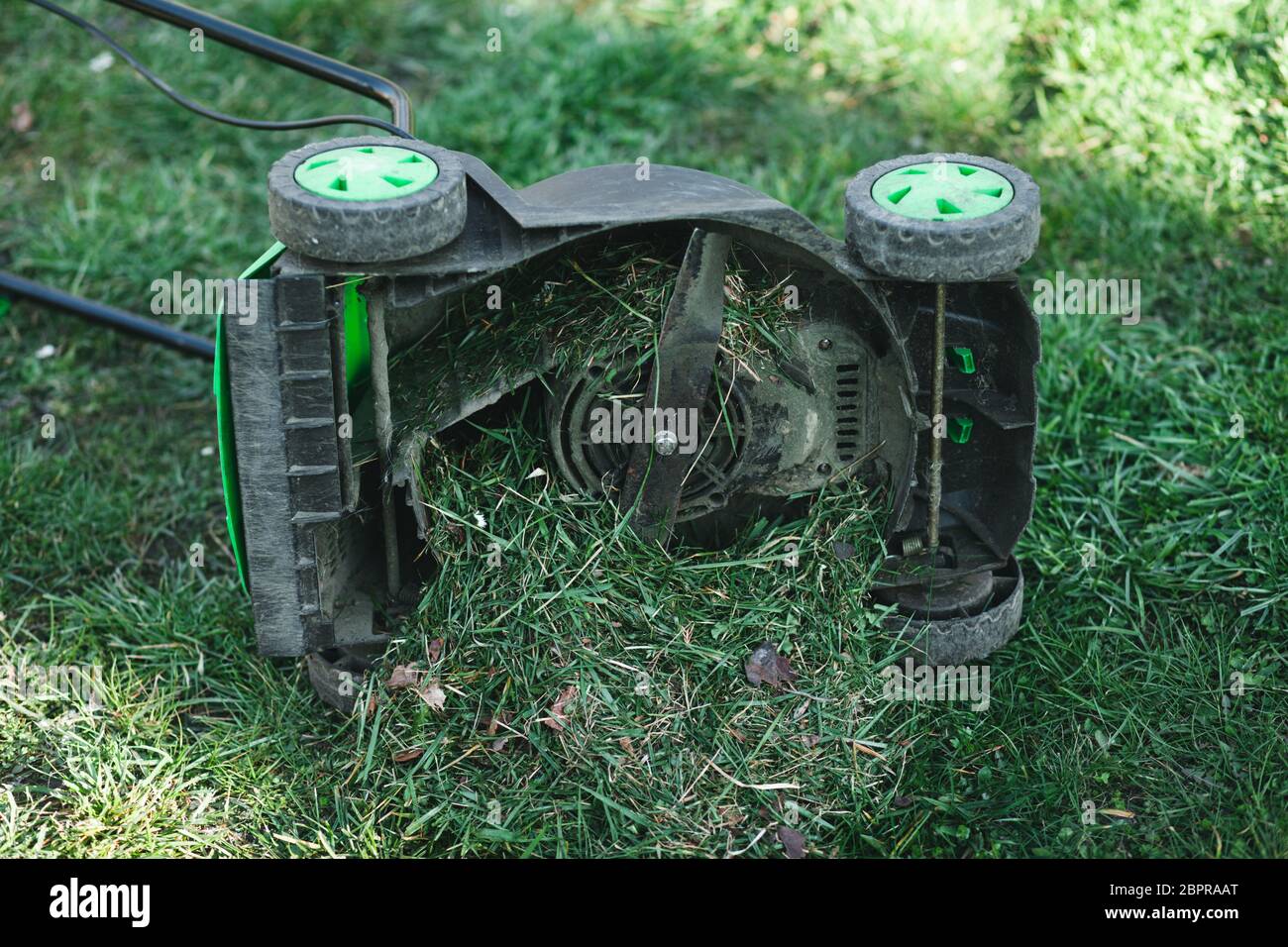 Lawn mower overflowing with grass lies on its side Stock Photo - Alamy