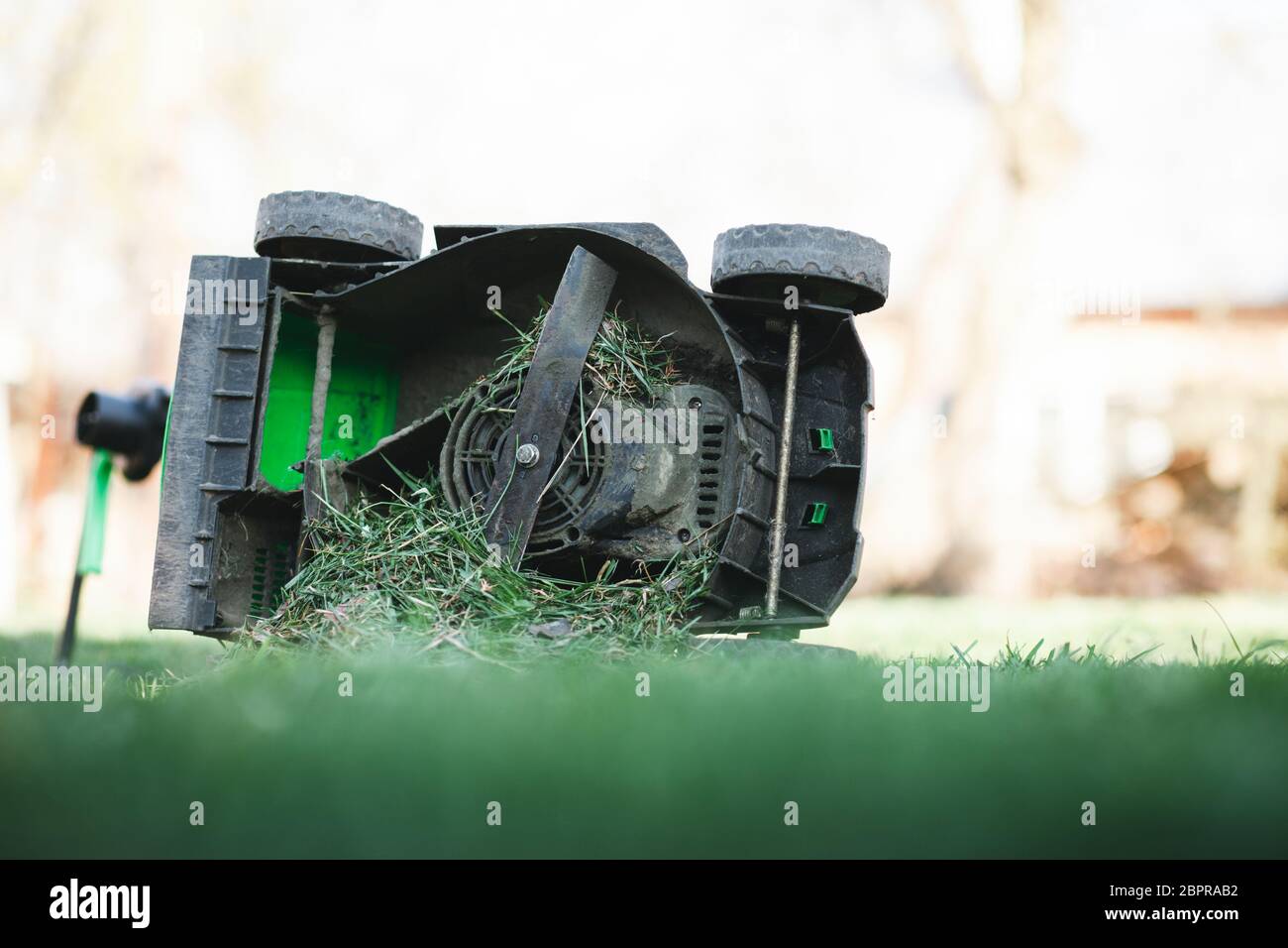 Lawn mower overflowing with grass lies on its side Stock Photo - Alamy