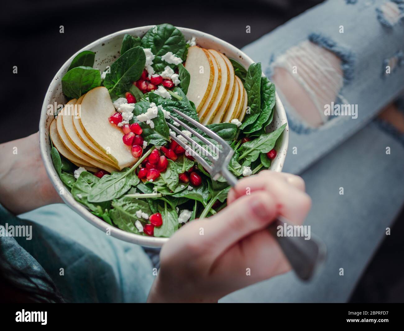 Woman in jeans holding vegan salad bowl with spinach, pear, pomegranate ...