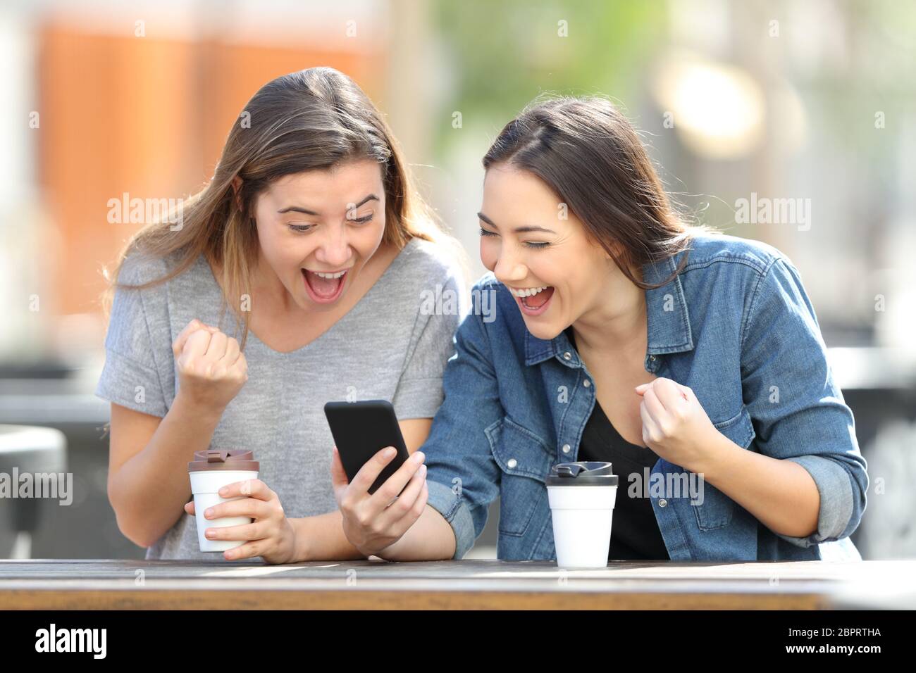 Two excited friends celebrating online good news checking phone in a ...