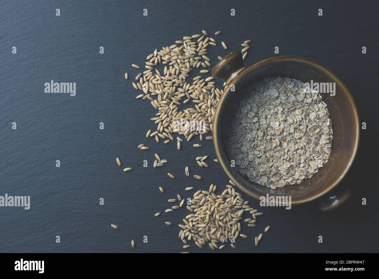 Peeled oats and oat meal on a dark stone table, healthy food concept ...